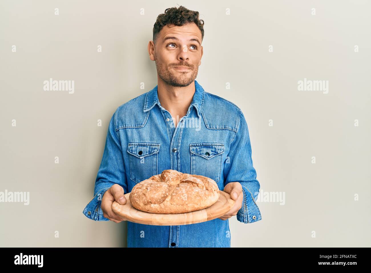 Young hispanic man holding bread smiling looking to the side and ...