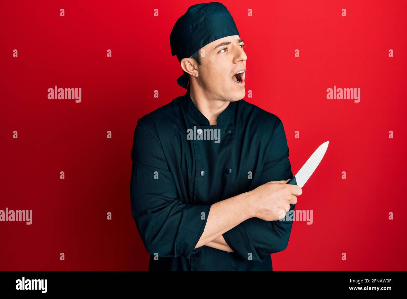 Handsome young man wearing professional cook uniform holding knife ...