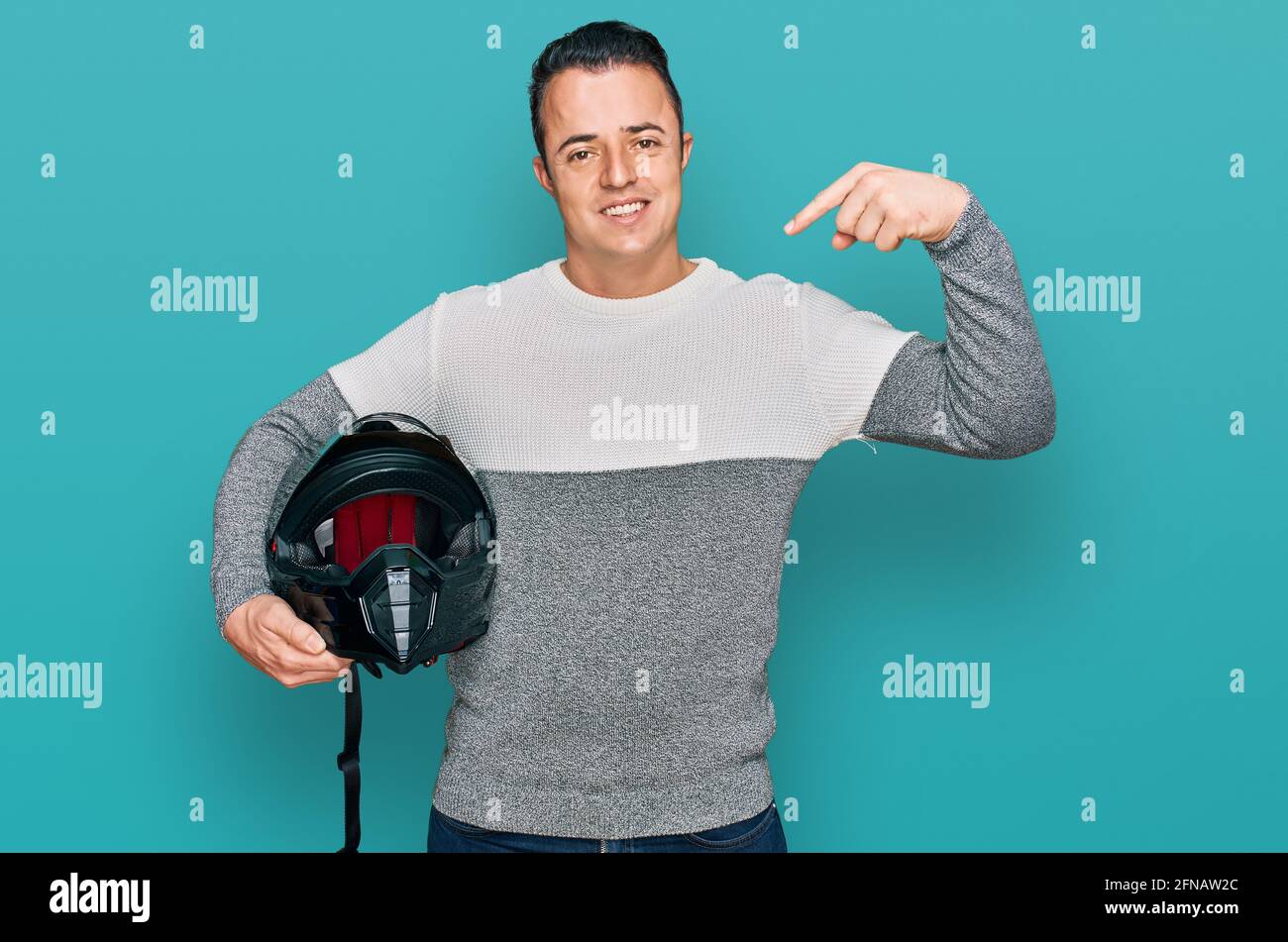 Handsome young man holding motorcycle helmet pointing finger to one ...