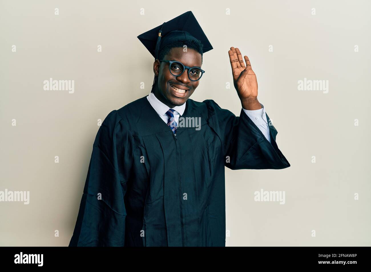 Handsome black man wearing graduation cap and ceremony robe waiving ...