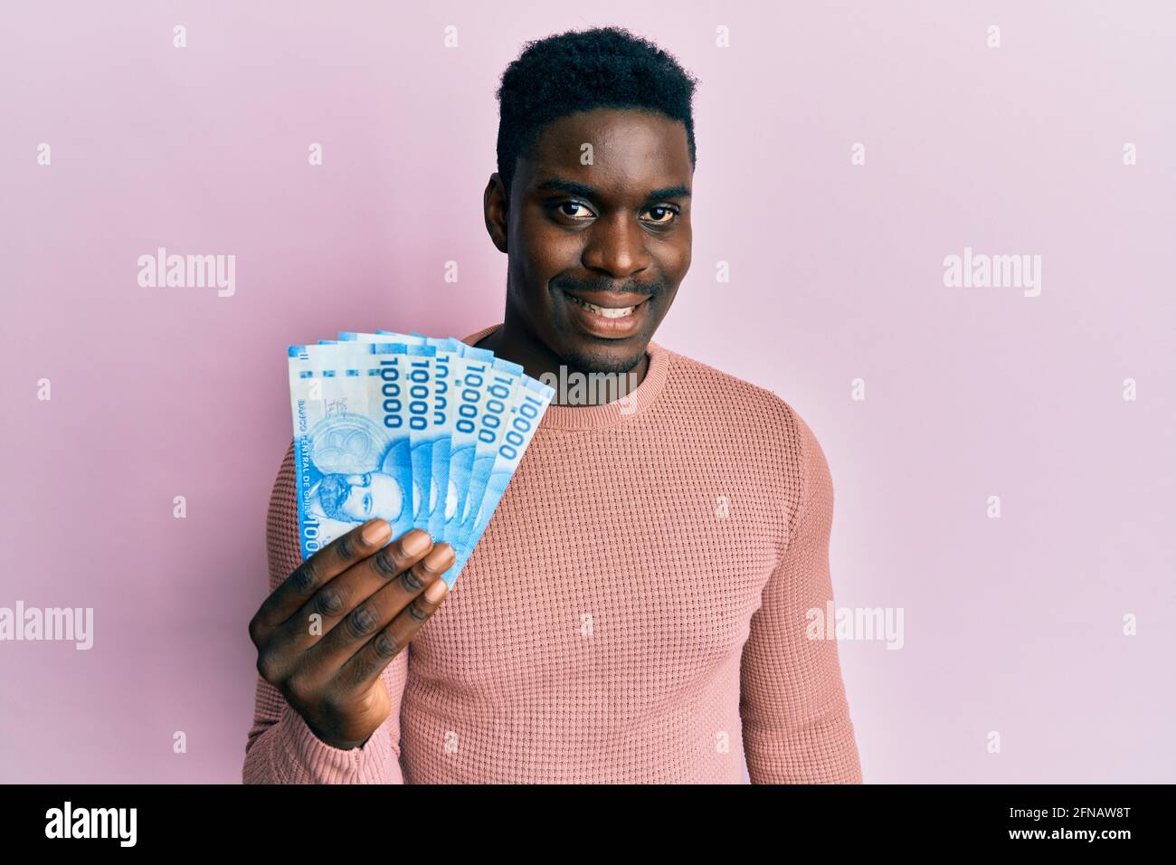 Handsome black man holding 10000 chilean pesos looking positive and ...