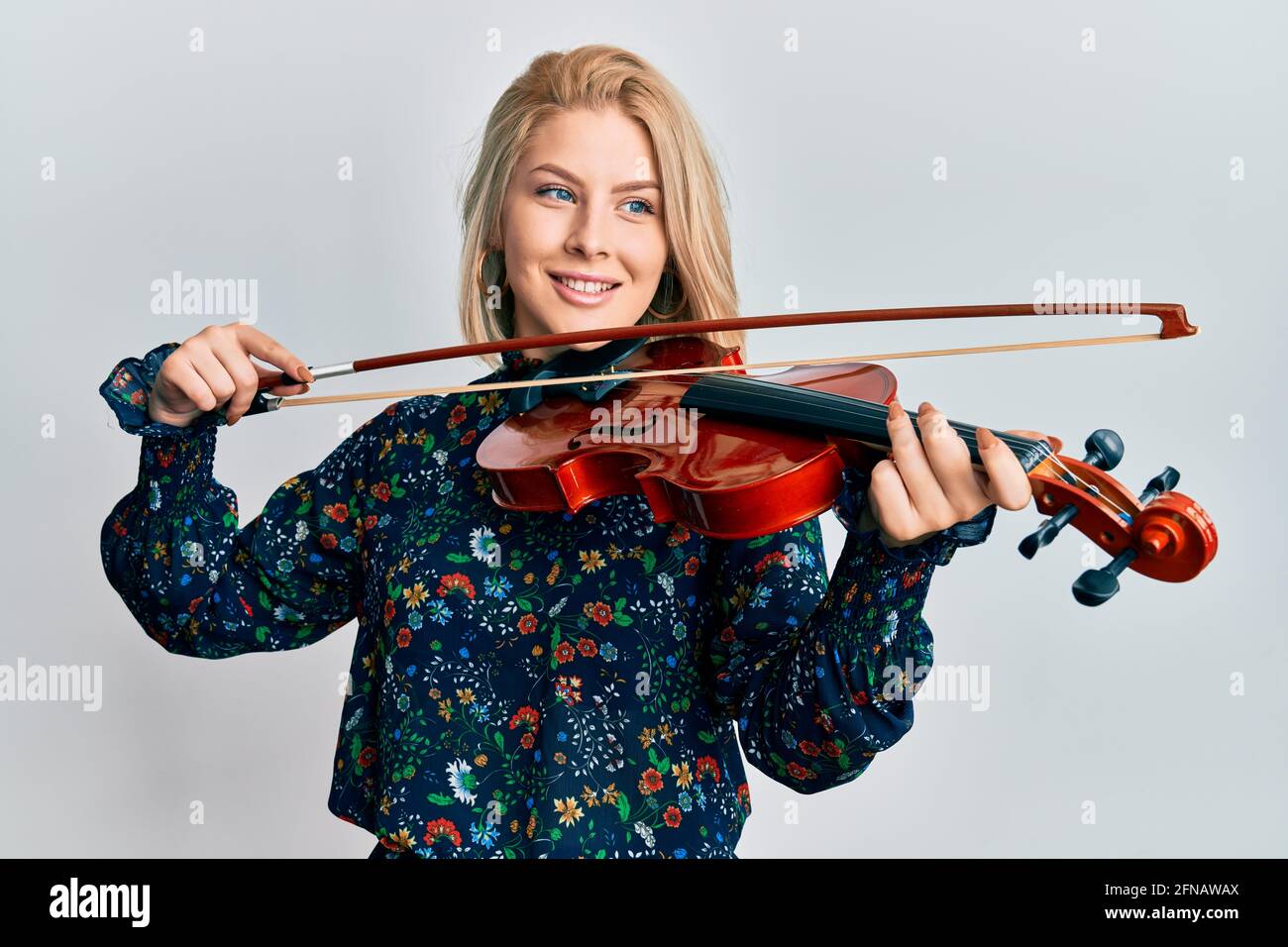Young blonde woman playing violin smiling looking to the side and ...