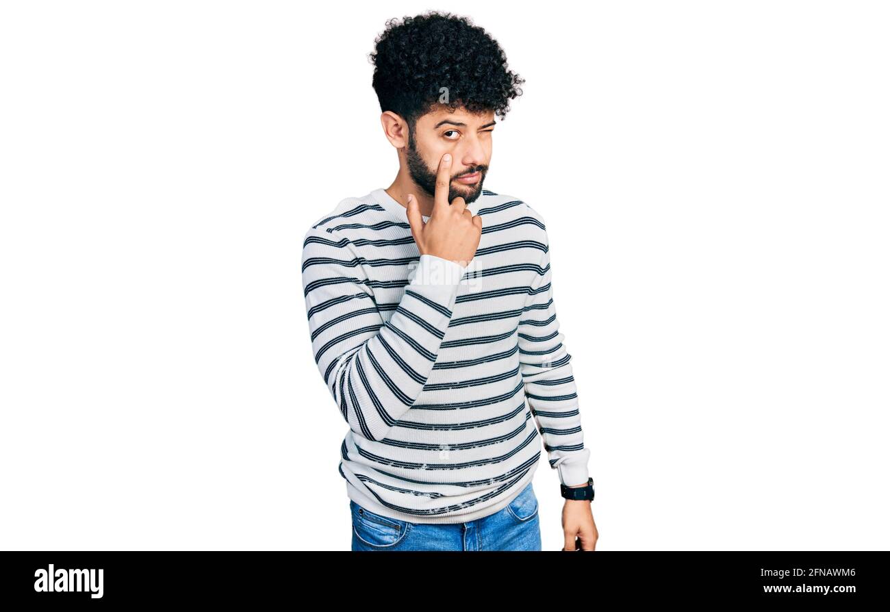Young arab man with beard wearing casual striped sweater pointing to ...