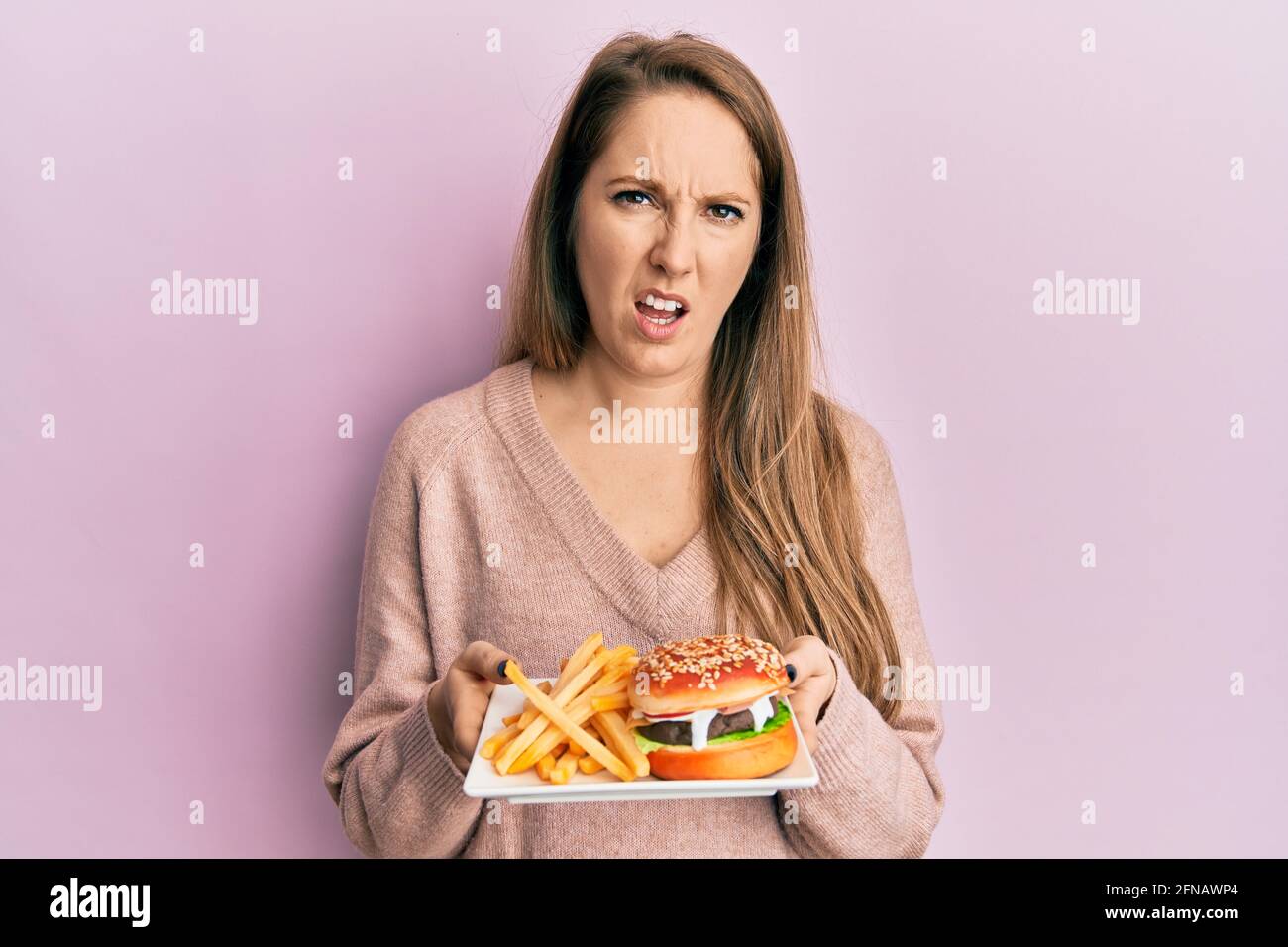 Young blonde woman eating a tasty classic burger with fries in shock ...