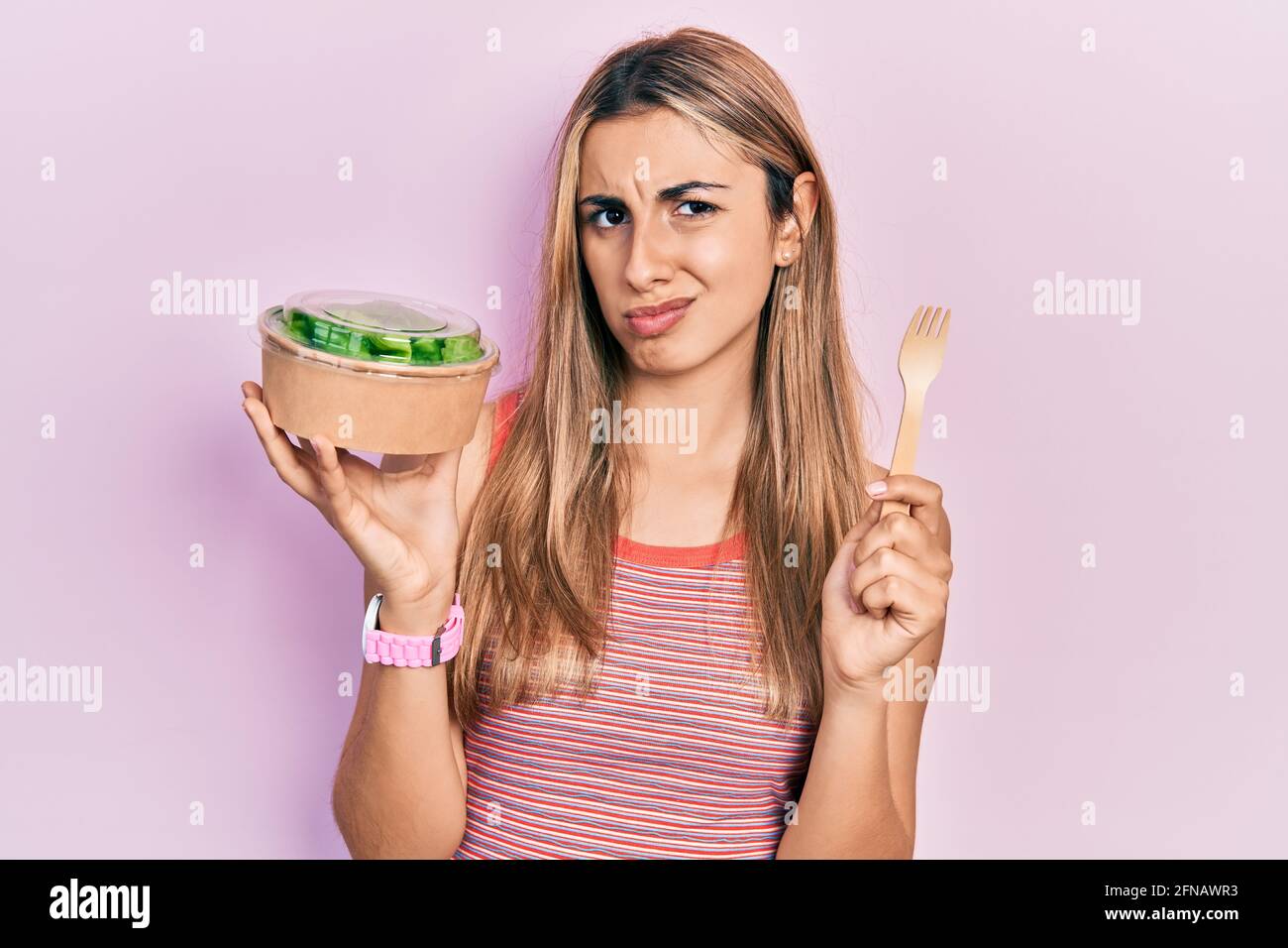 Beautiful hispanic woman eating salad clueless and confused expression ...