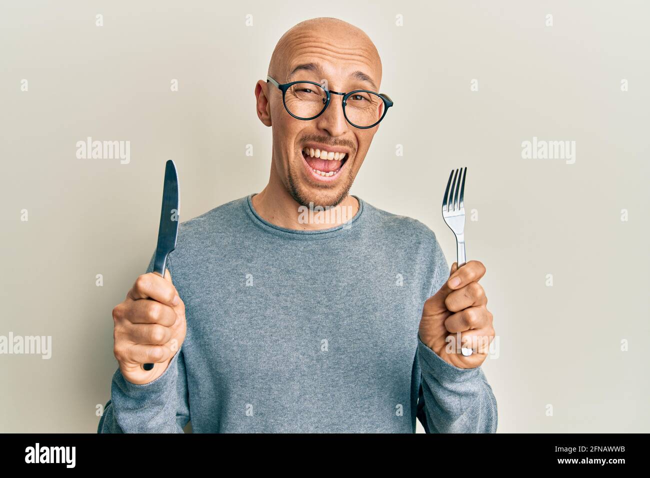 Bald man with beard holding fork and knife ready to eat smiling and ...
