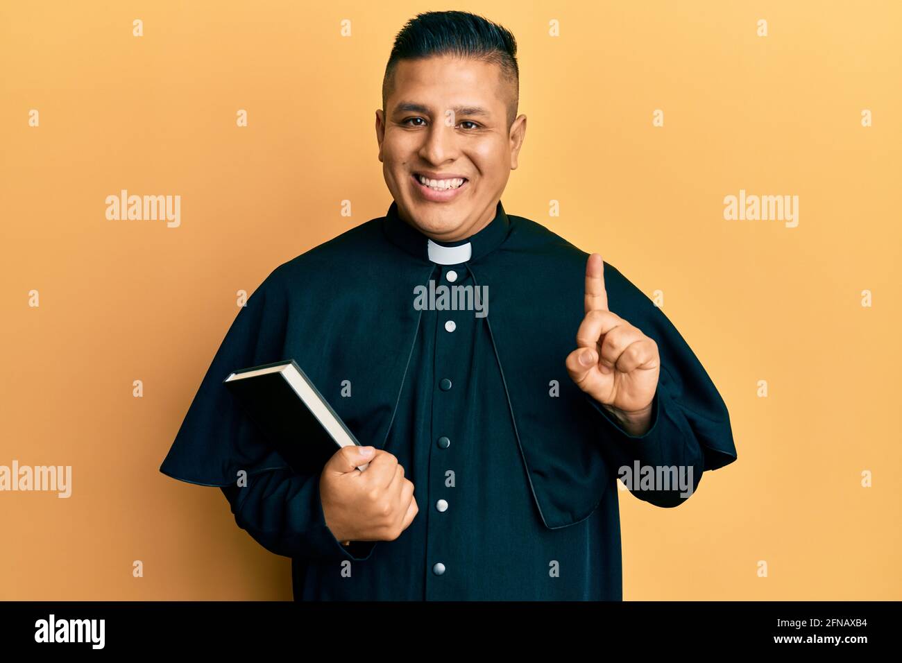 Young latin priest man holding bible smiling with an idea or question ...