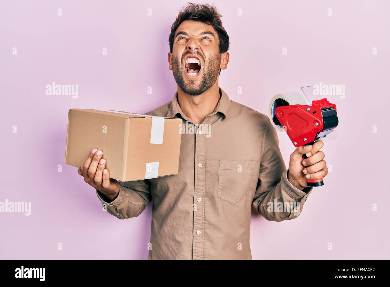 Handsome man with beard holding packing tape holding cardboard angry ...