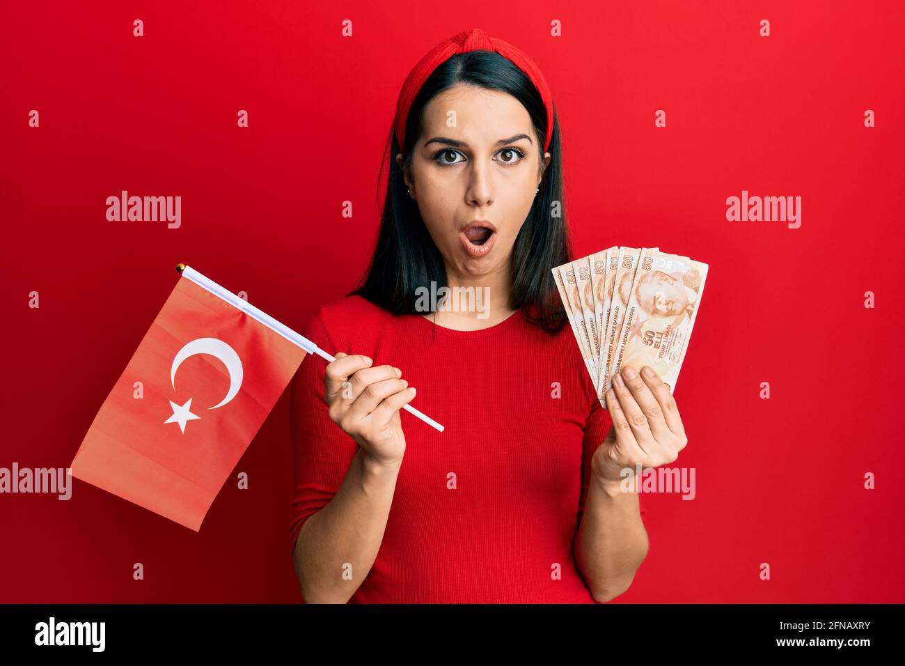 Young hispanic woman holding turkey flag and liras banknotes afraid and ...