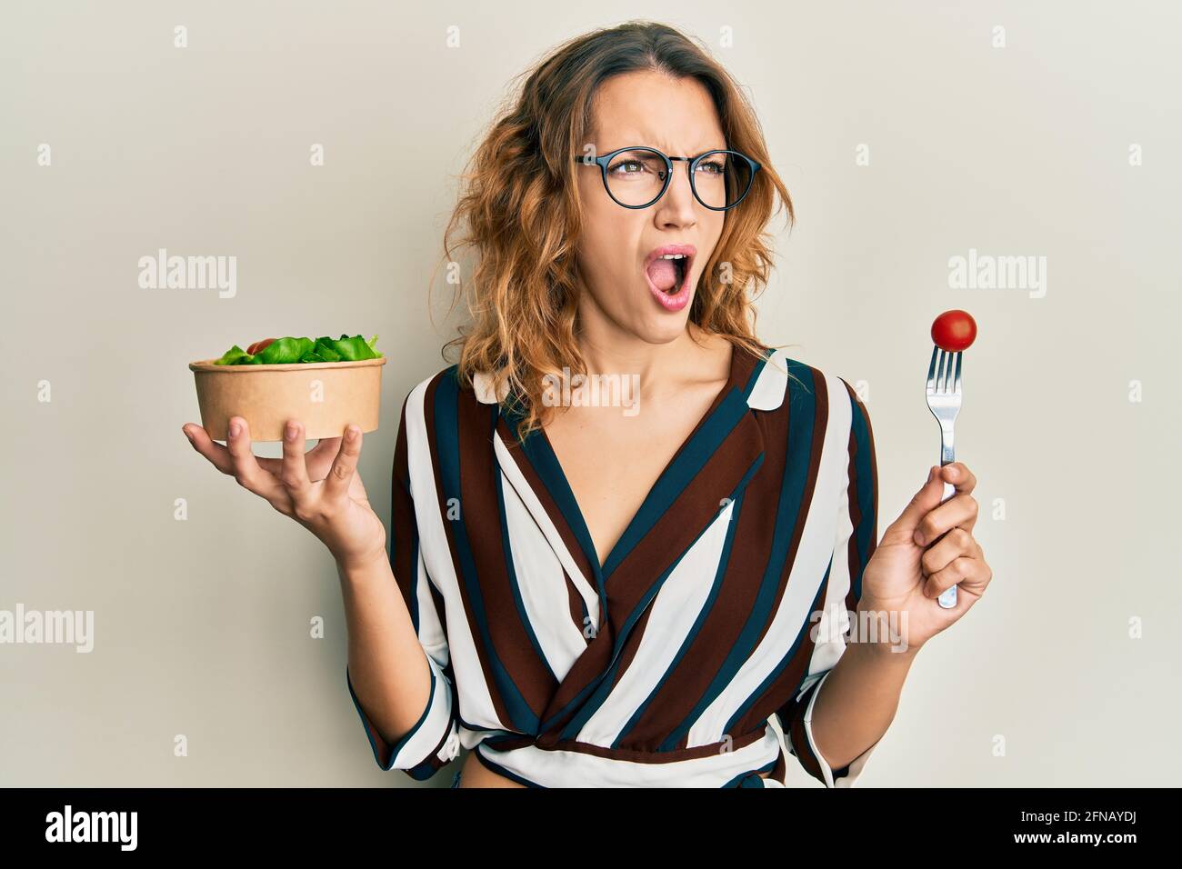 Young caucasian woman wearing business clothes eating salad angry and ...