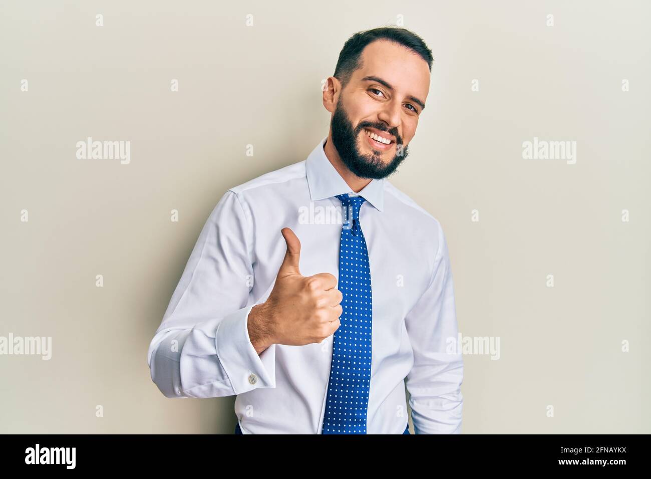 Young man with beard wearing business tie doing happy thumbs up gesture ...