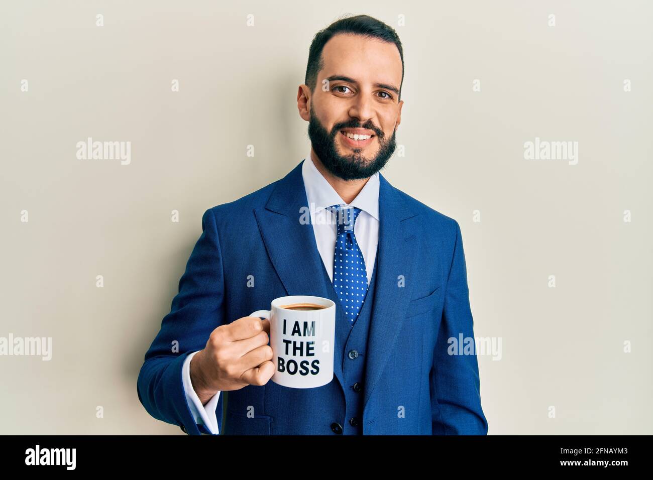 Young man with beard drinking from i am the boss coffee cup looking ...