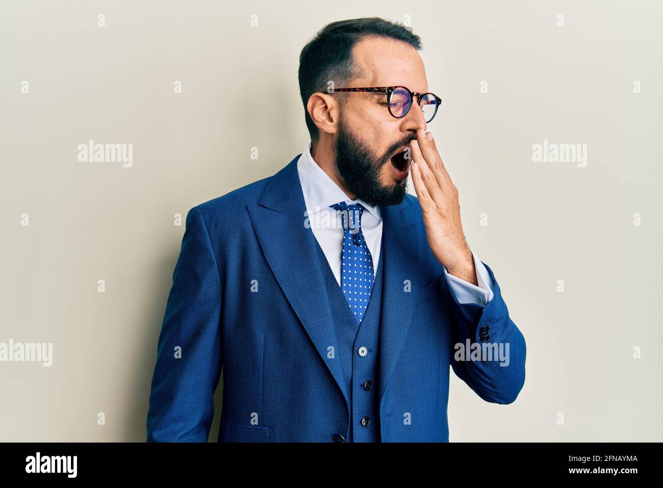 Young man with beard wearing business suit and tie bored yawning tired ...