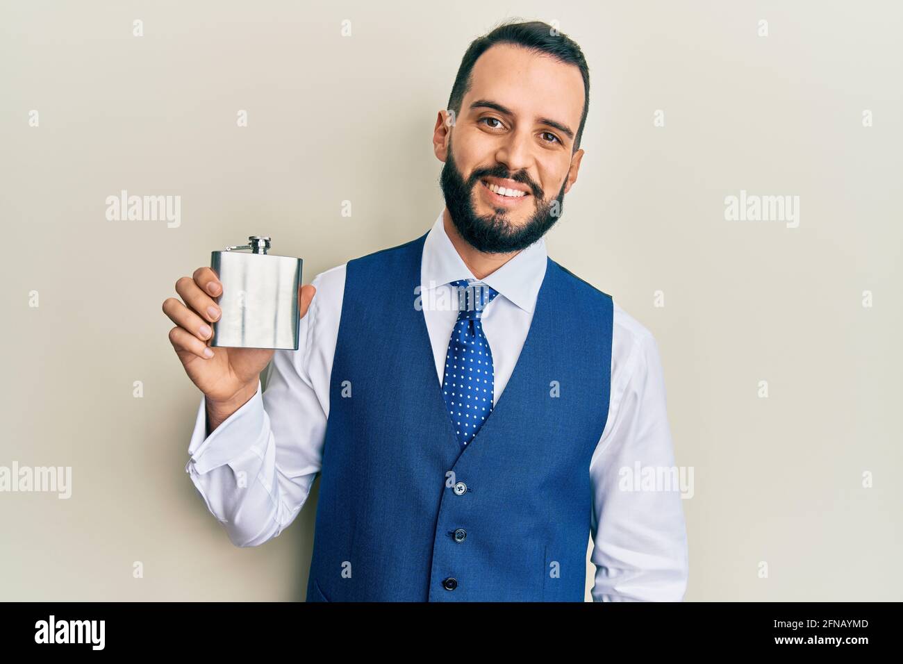 Young man with beard drinking whiskey from flask looking positive and ...
