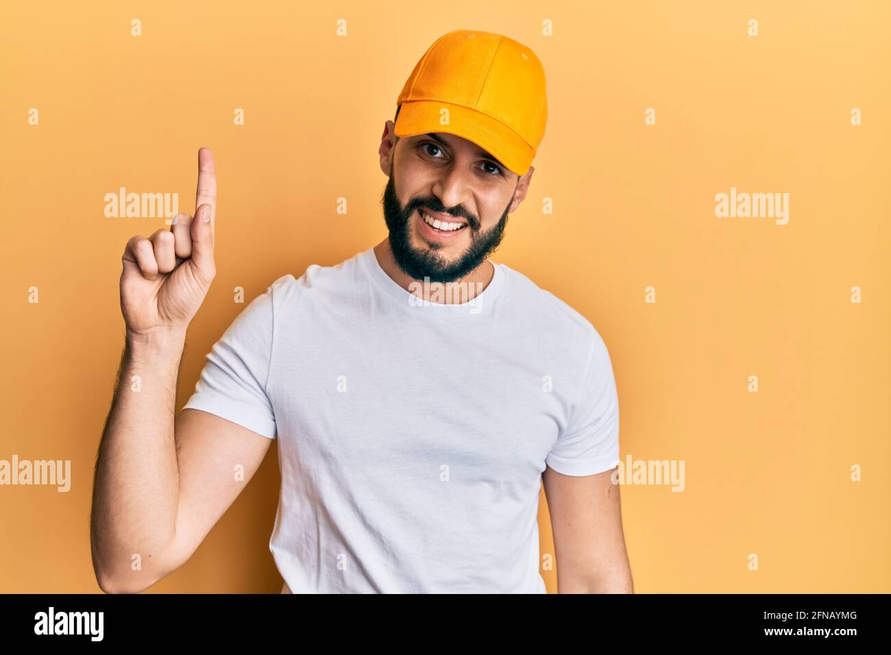 Young man with beard wearing yellow cap smiling with an idea or ...
