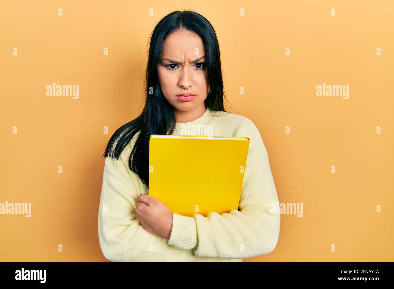 Beautiful hispanic woman with nose piercing holding book skeptic and ...