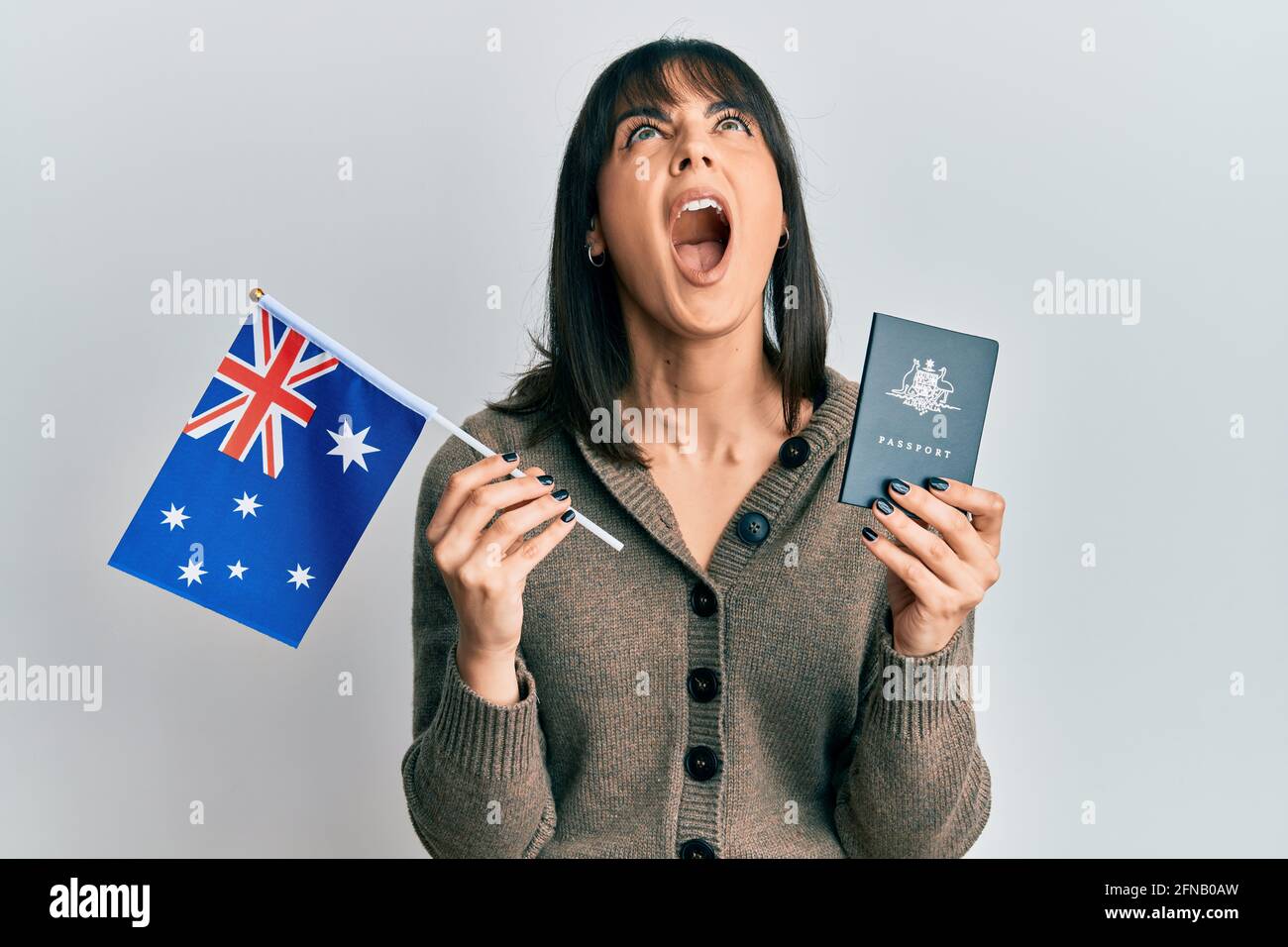 Young hispanic woman holding australian flag and passport angry and mad ...