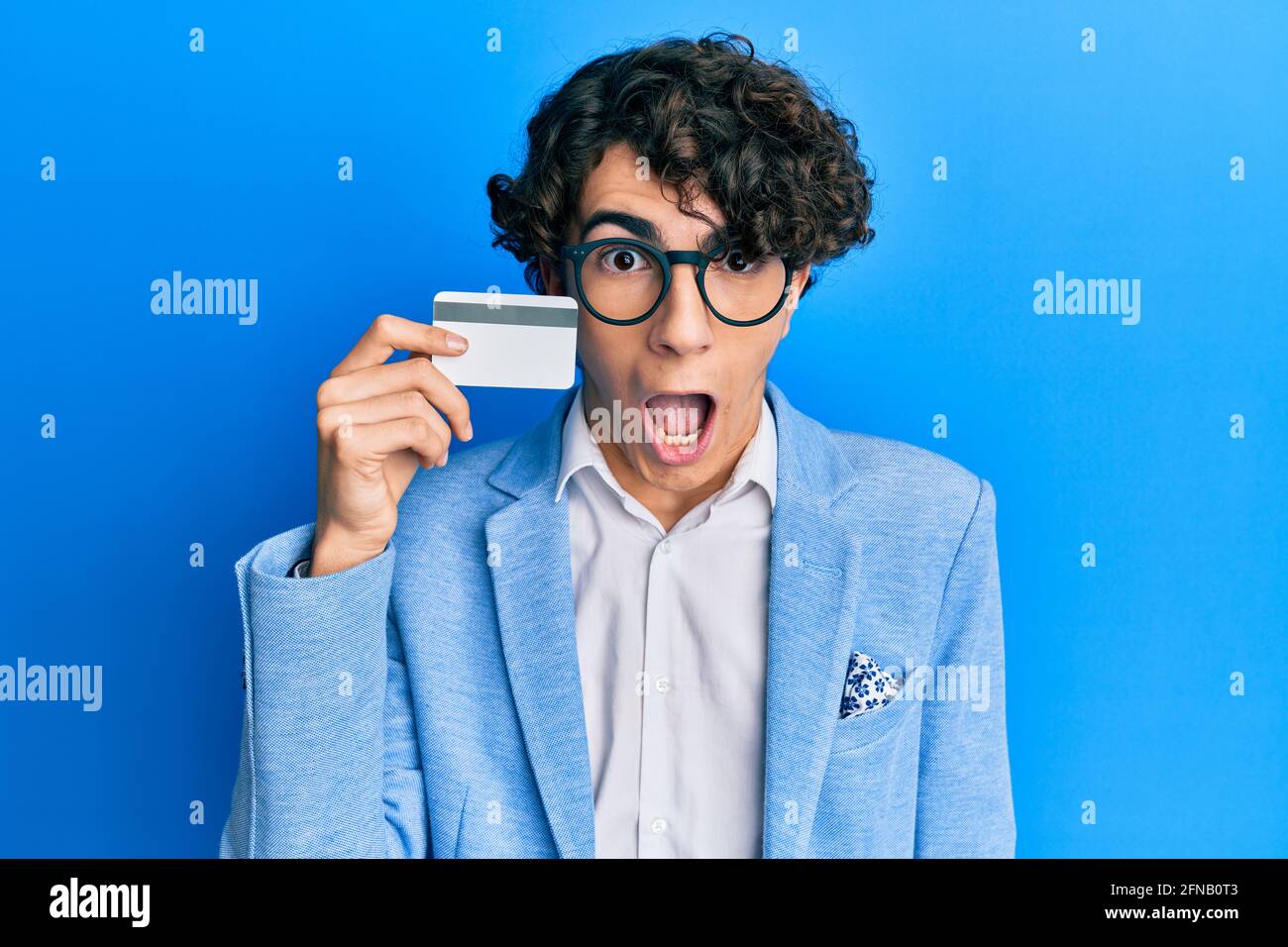 Hispanic young man holding credit card scared and amazed with open ...