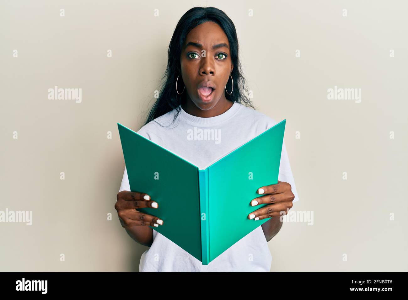 Young african american woman reading book afraid and shocked with ...