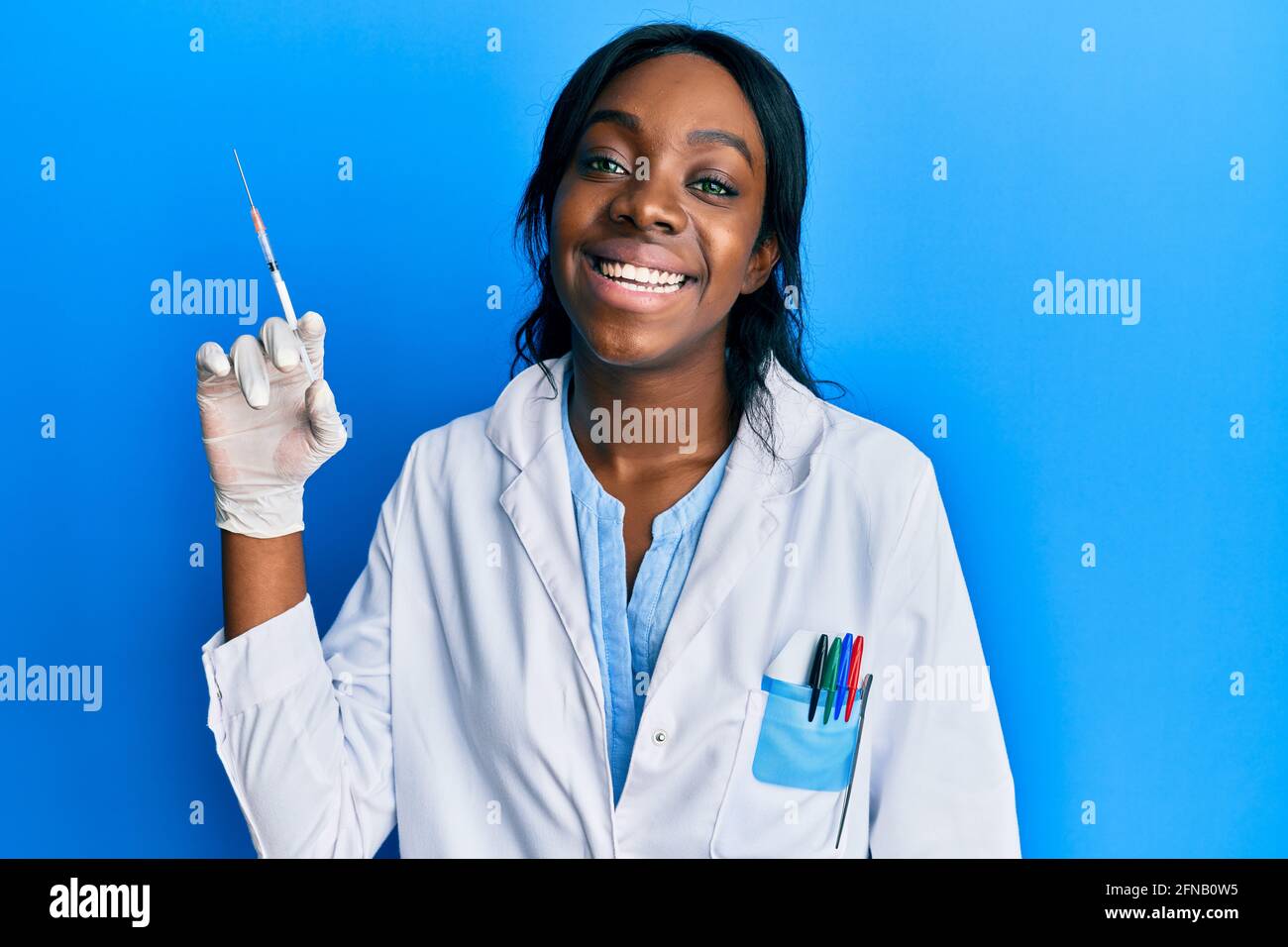 Young african american woman wearing scientist uniform holding syringe looking positive and ...