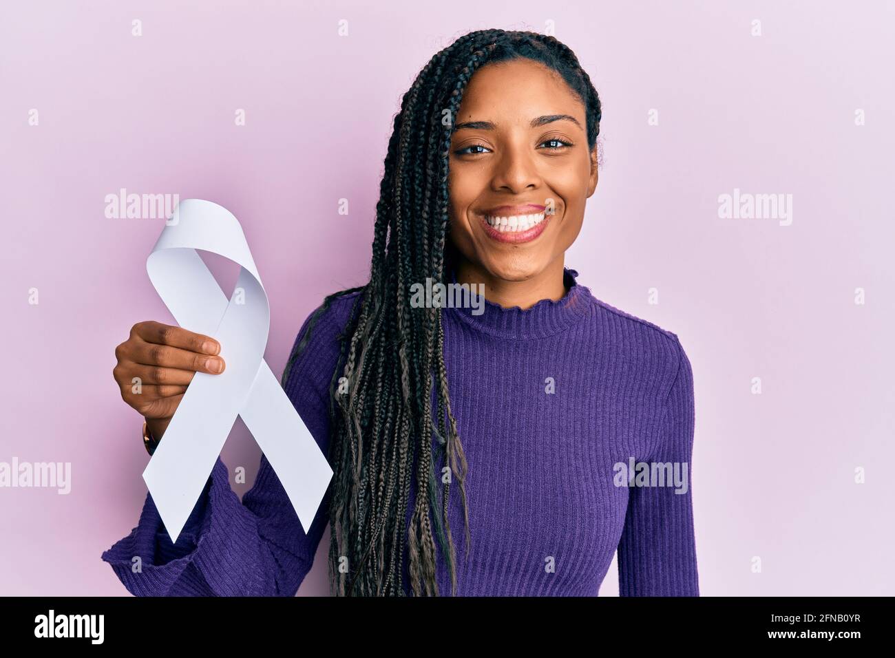 African american woman holding white ribbon looking positive and happy ...