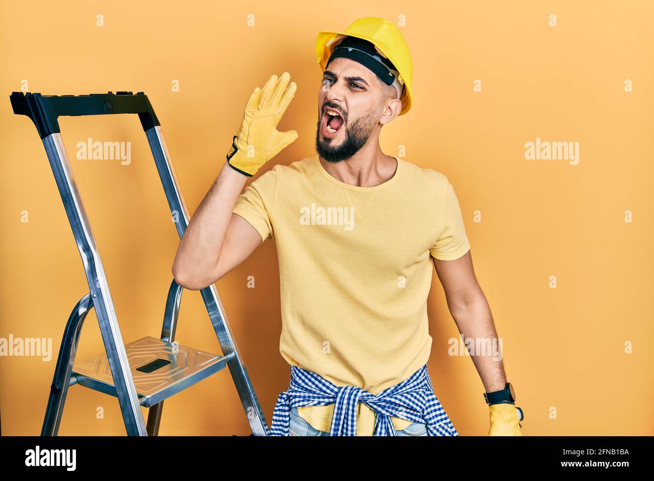 Handsome man with beard by construction stairs wearing hardhat shouting ...