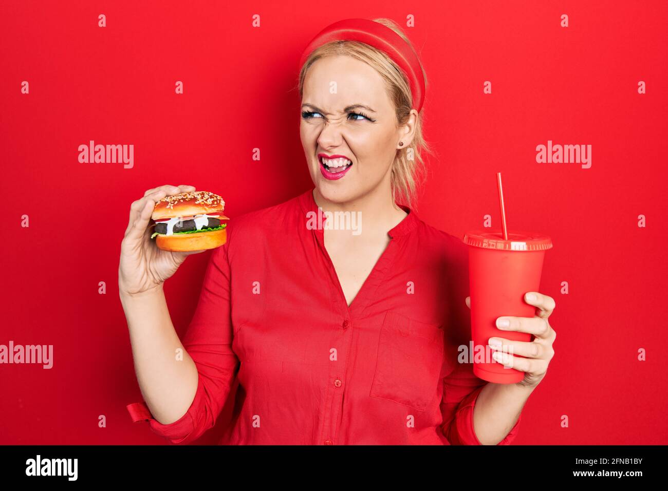 Young blonde woman eating a tasty classic burger with fries and soda ...