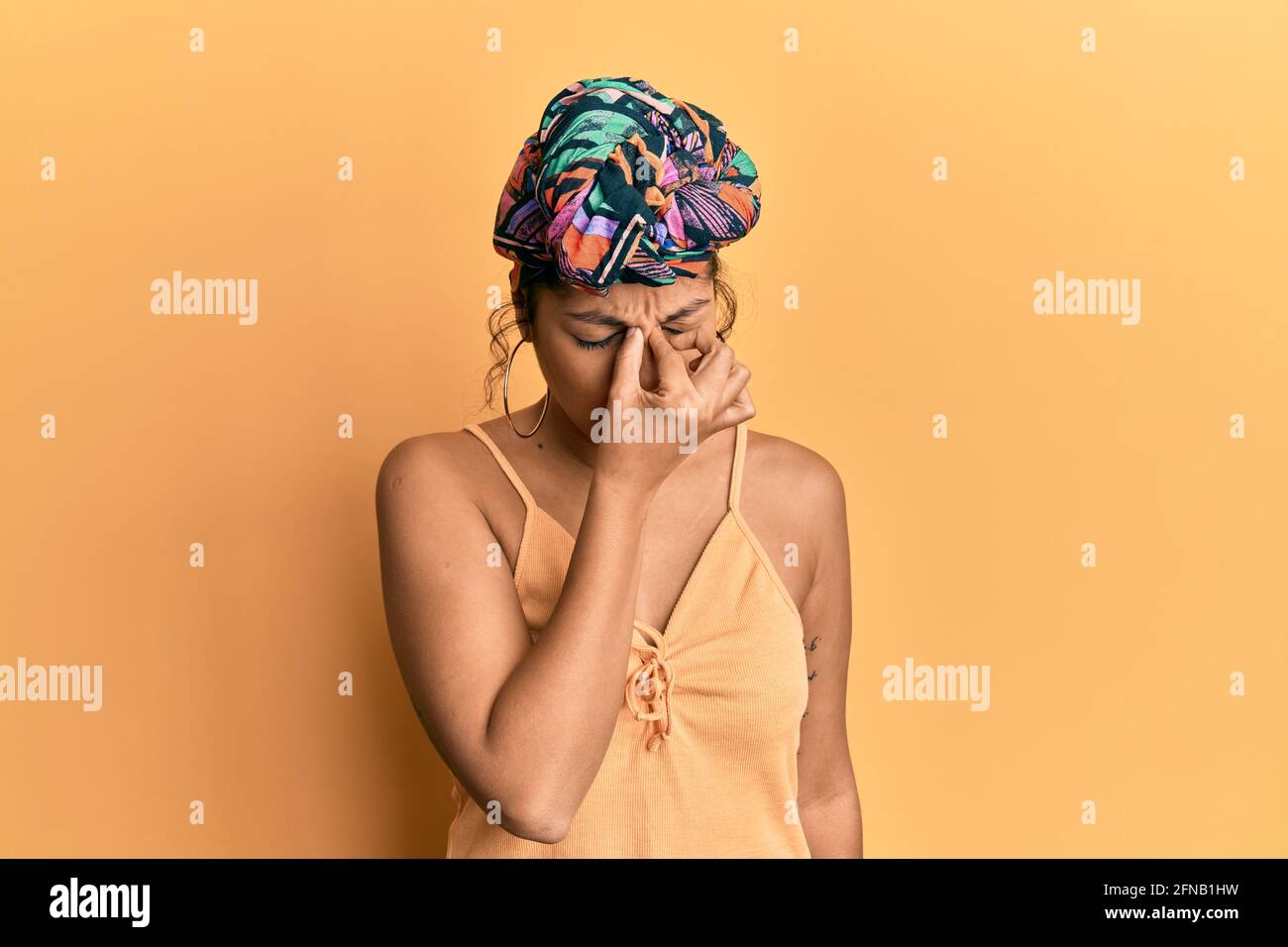 Young hispanic girl wearing hair turban over yellow background tired ...