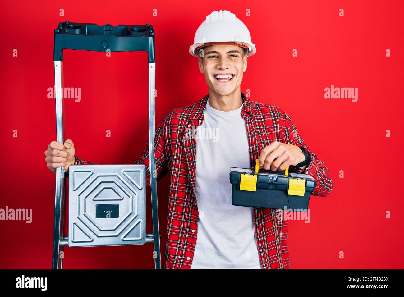 Young hispanic man holding tools box wearing hardhat by construction ...