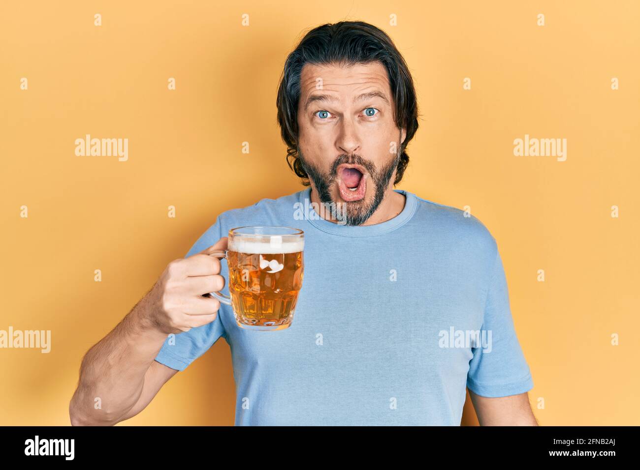 Middle age caucasian man drinking a jar of beer scared and amazed with ...