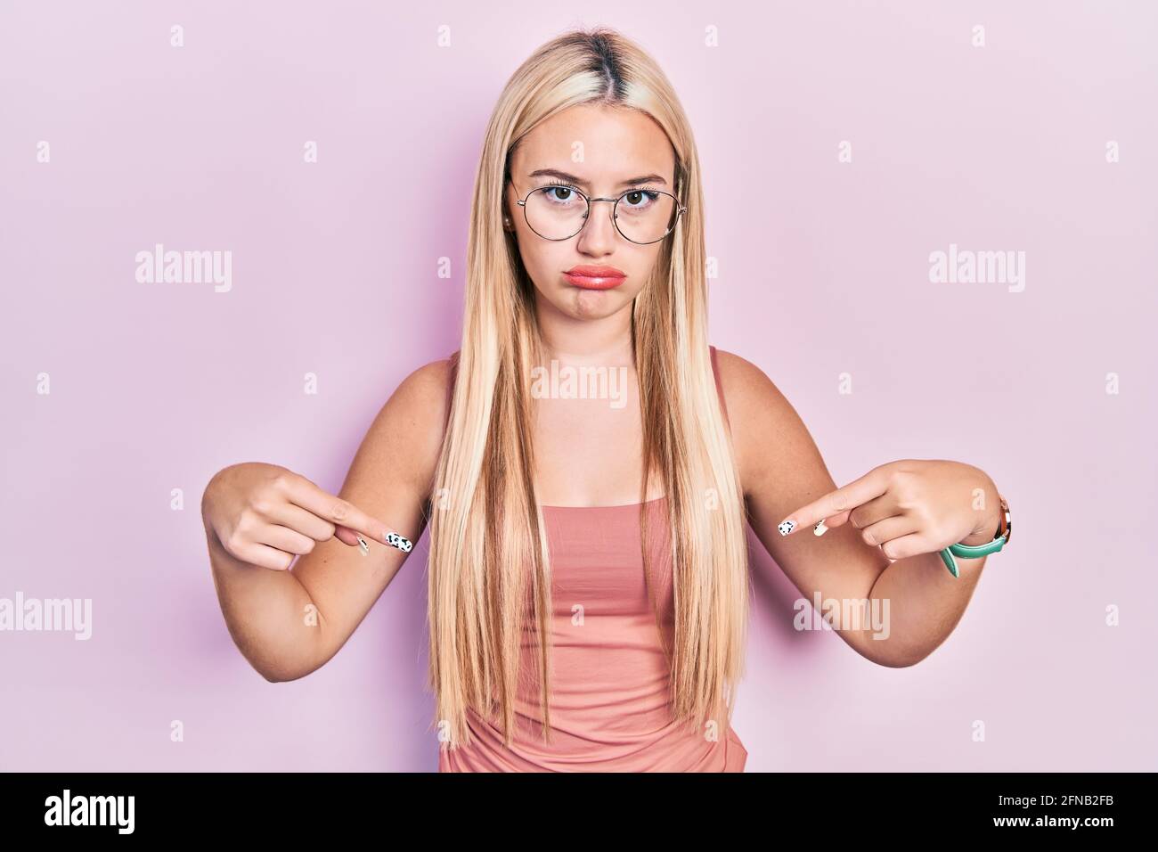 Young blonde girl wearing casual clothes pointing down looking sad and ...