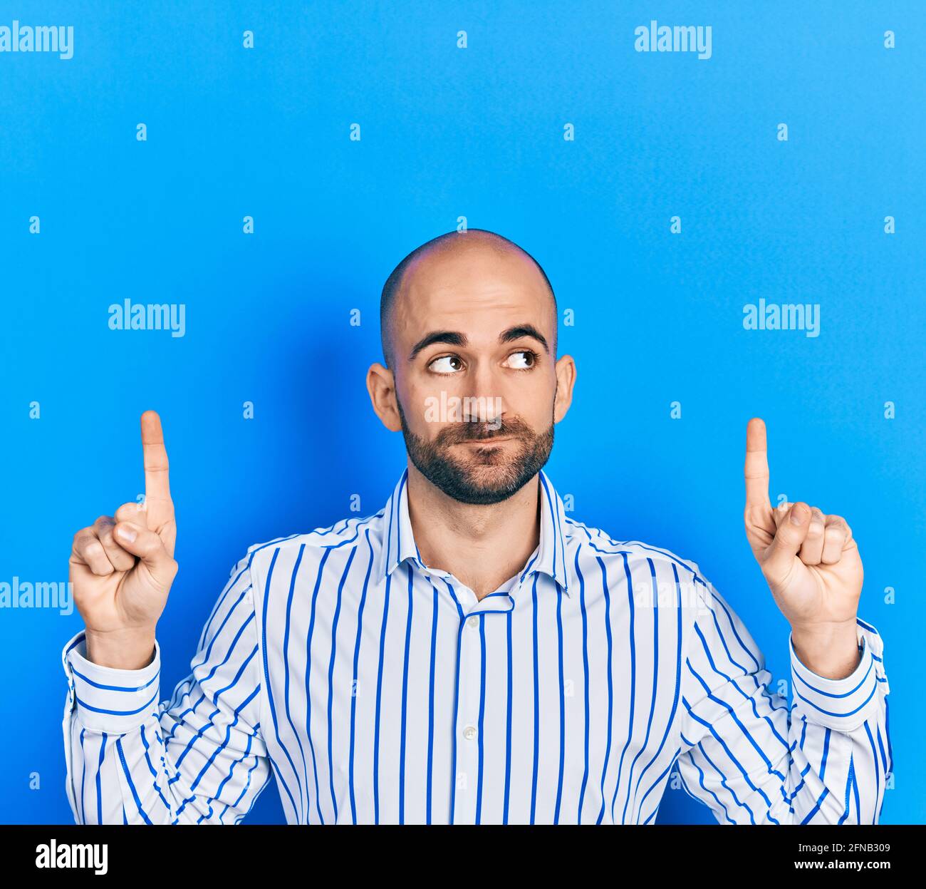 Young bald man pointing up with fingers smiling looking to the side and ...