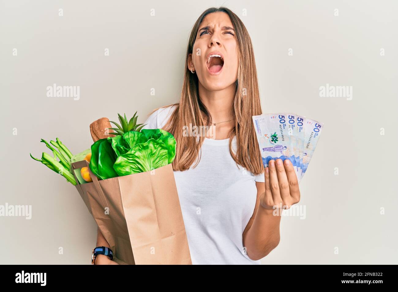 Brunette young woman holding groceries and 50 colombian pesos banknotes ...