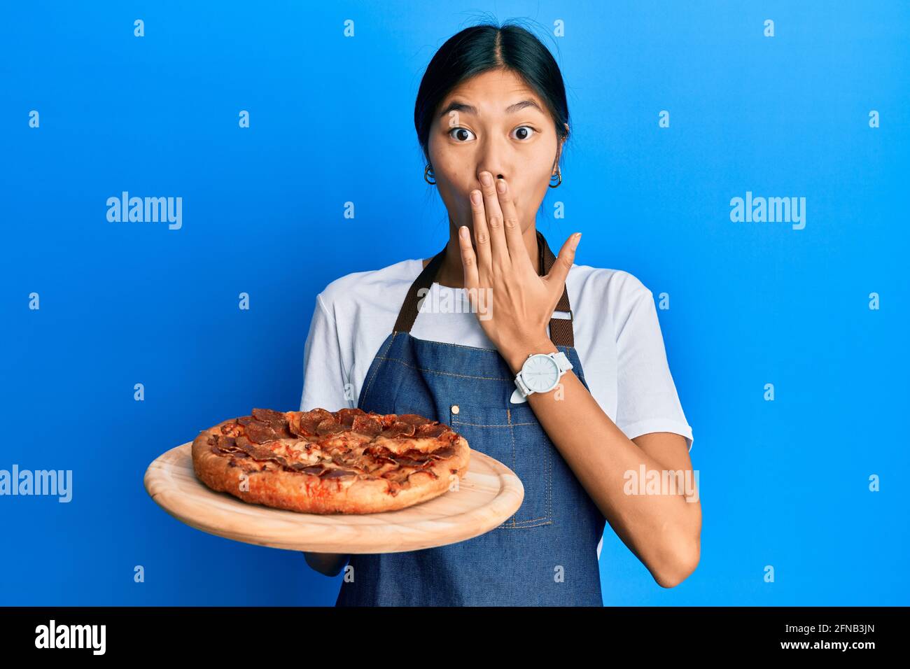 Young chinese woman wearing waiter apron holding italian pizza covering ...