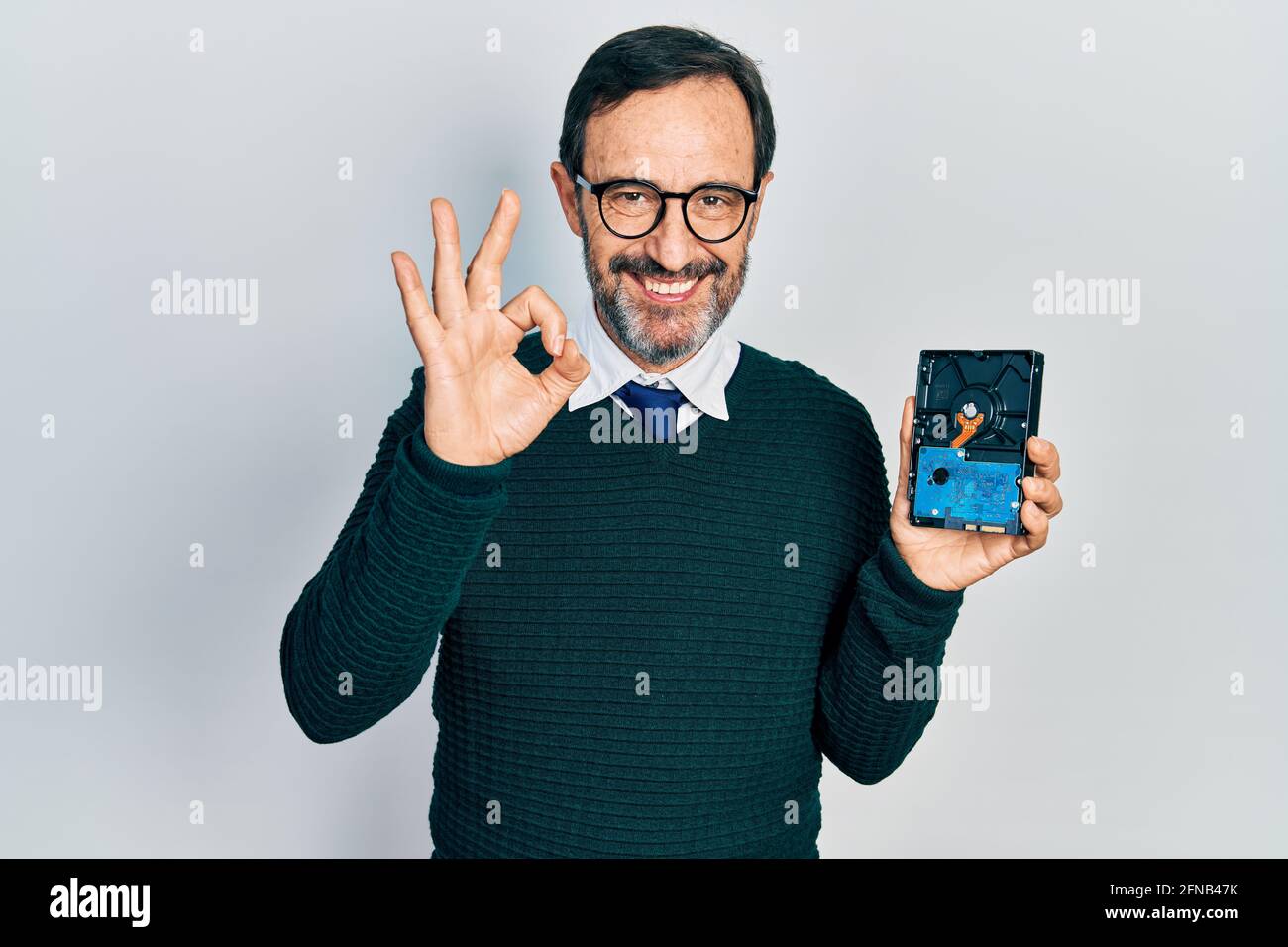 Middle age hispanic man holding hdd disk doing ok sign with fingers ...