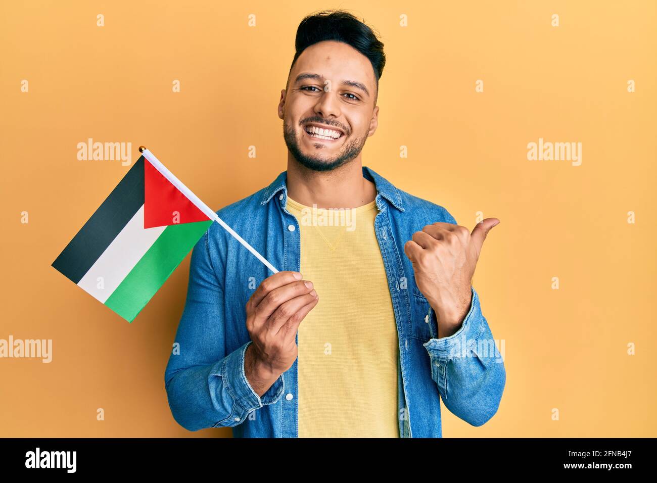 Young arab man holding palestine flag pointing thumb up to the side ...