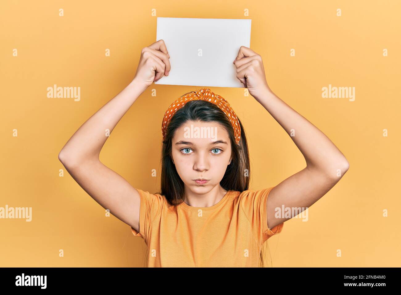 Young brunette girl holding blank empty banner over head puffing cheeks ...