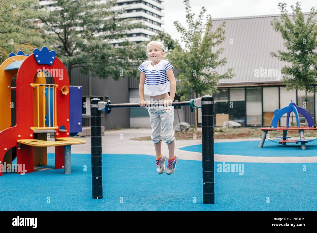 Happy smiling young girl exercising on children pull-ups bar outdoors ...