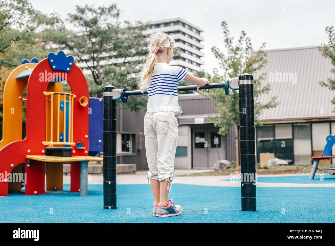 Happy smiling young girl exercising on children pull-ups bar outdoor at ...