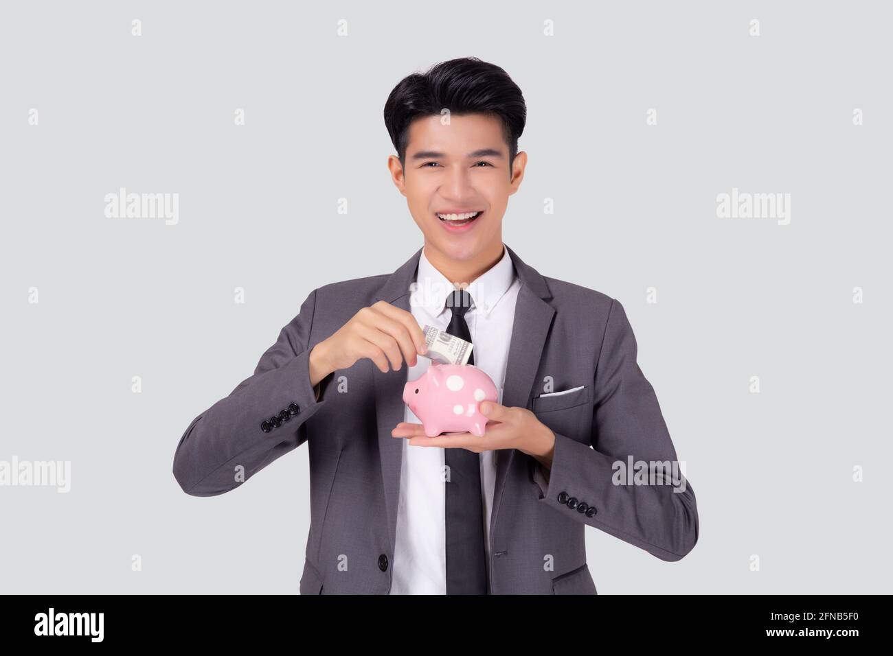Young asian businessman in suit deposit money dollar with piggy bank ...