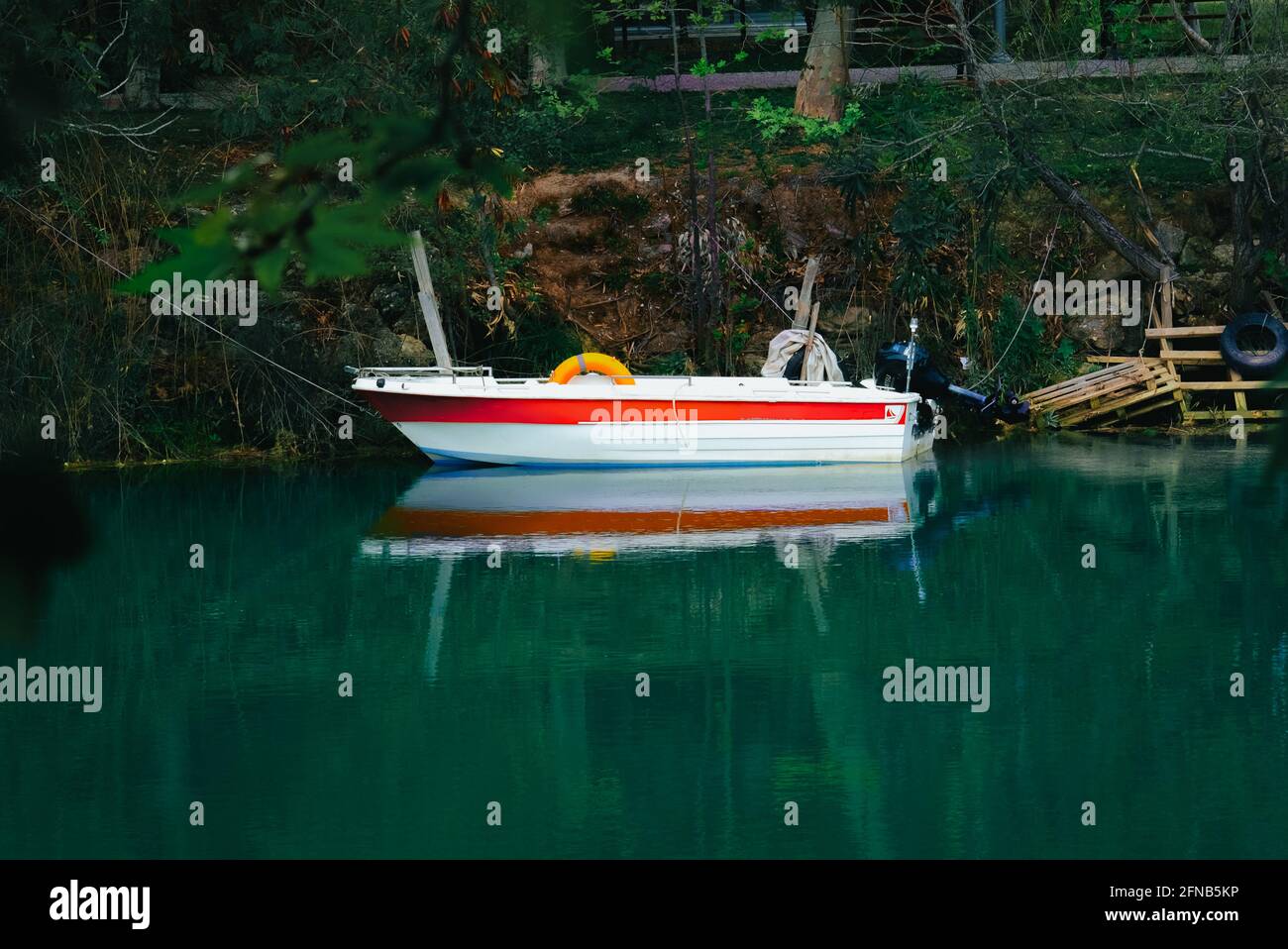 a simple fishing boat on a narrow river with it's reflection on water ...