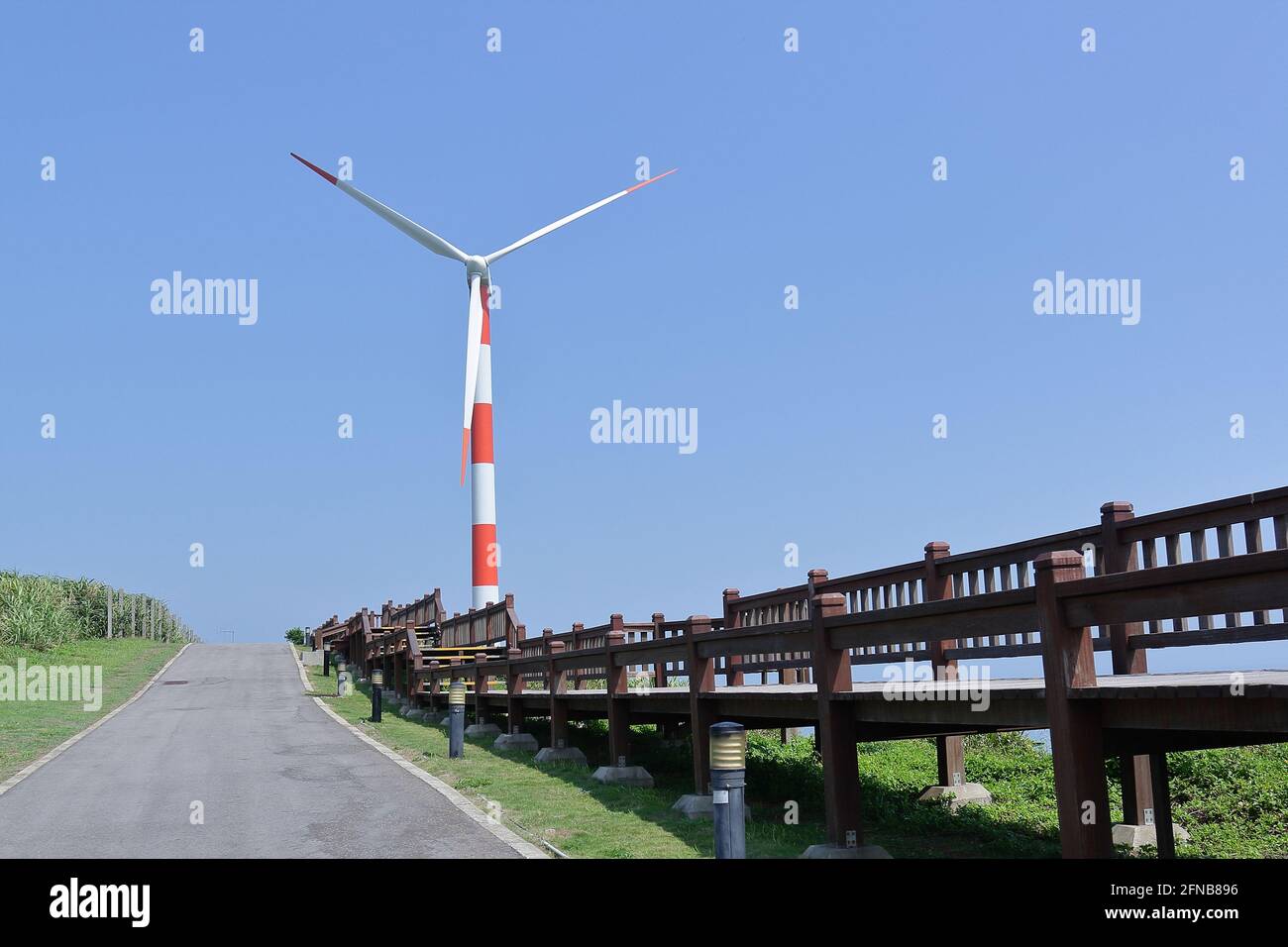 a orange-white wind turbine located by the coast, blue sky as ...