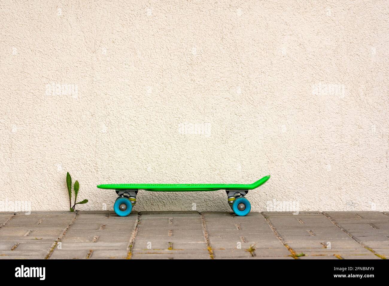 Green plastic skateboard on the pavement against white wall. Copy space ...
