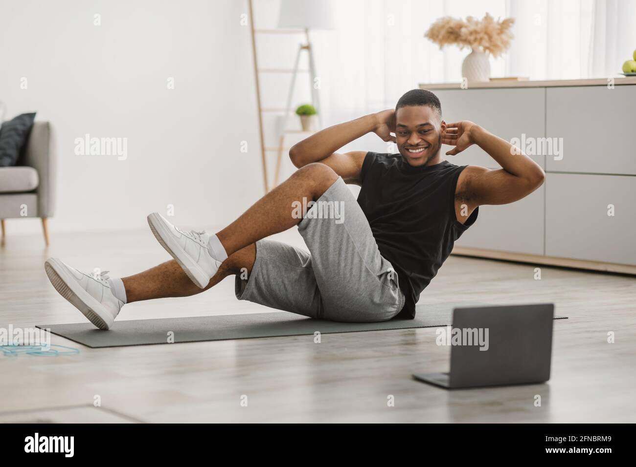 Happy Black Man Doing Elbow-To-Knee Abs Crunches At Laptop Indoor Stock ...