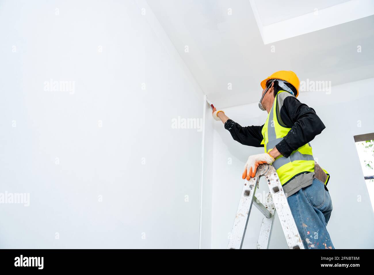 painter man painting the wall in an unfinished building, with paint ...
