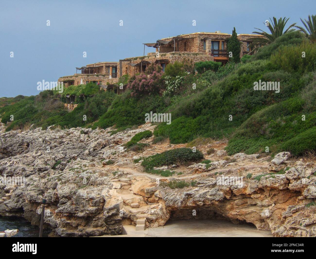 Beach houses built of orange sandstone on the rocky coast of Menorca ...