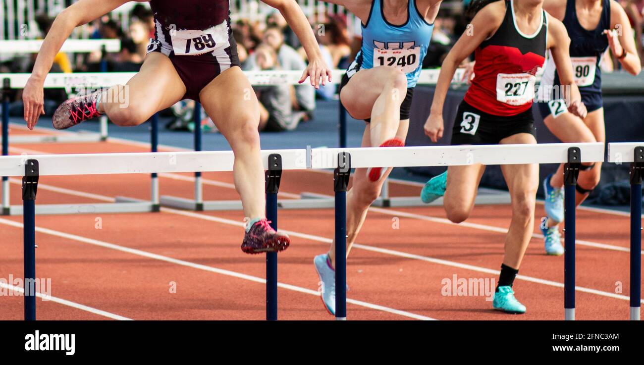 Front view of four high school girls running in a hurdle track and ...