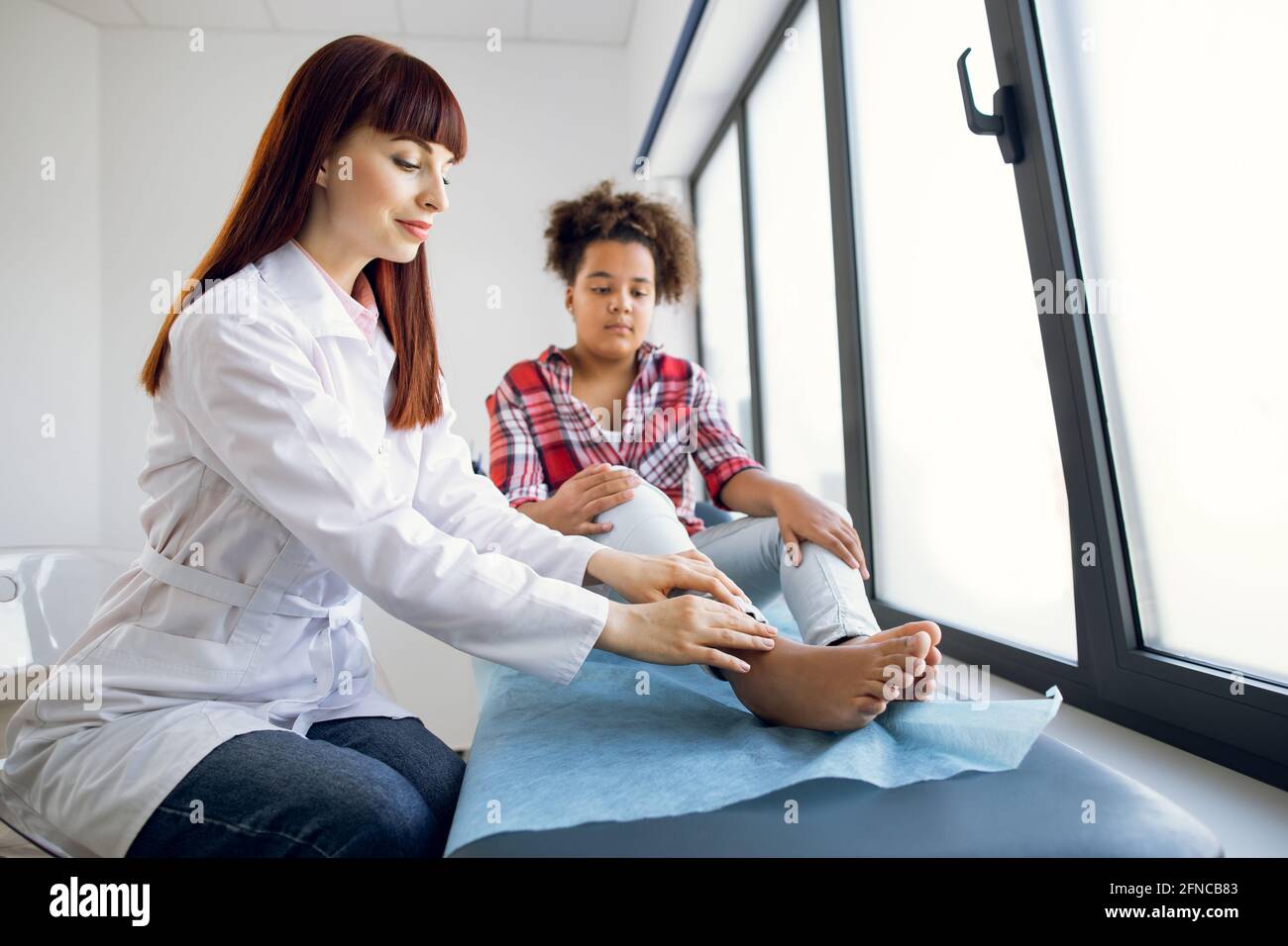 Young confident Caucasian woman doctor orthopedist examining feet of ...