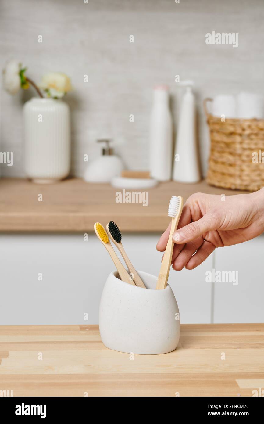 Female hand holding wooden toothbrush in a white cup in bathroom Stock ...