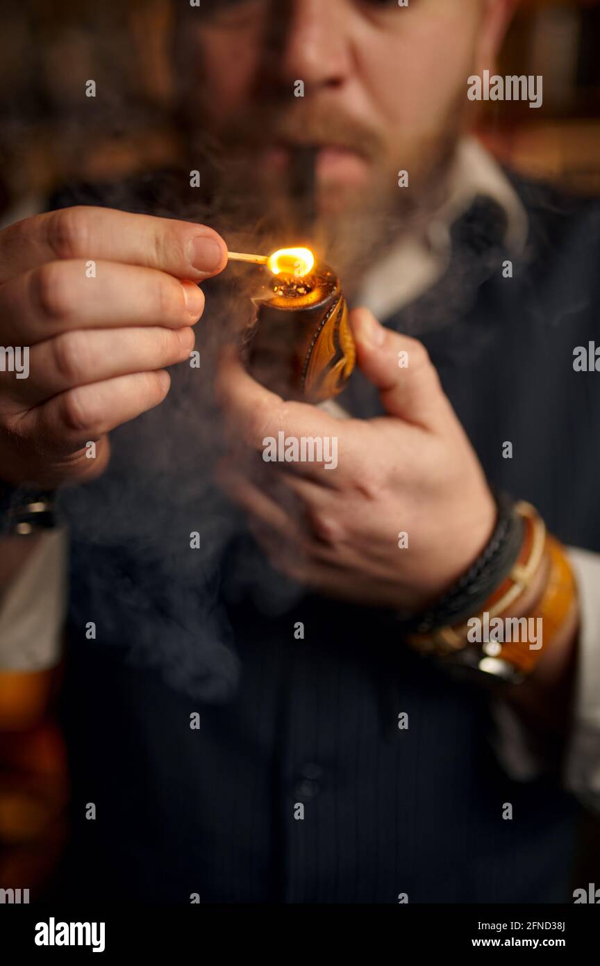 Bearded man lights smoking pipe with a match Stock Photo - Alamy